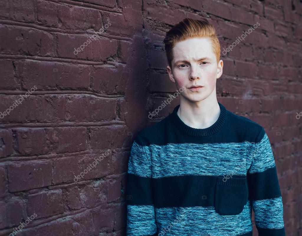 Jeune rousse homme en pull et jeans debout à côté d'un mur de briques ...