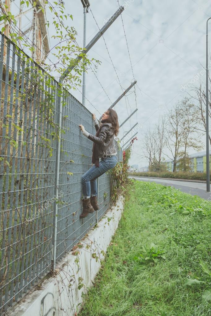 Beautiful young brunette climbing over a fence — Stock Photo © tinx ...