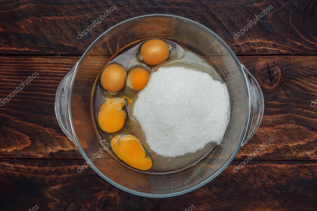 Huevos y yema con azúcar en un tazón de vidrio sobre un fondo de madera ...