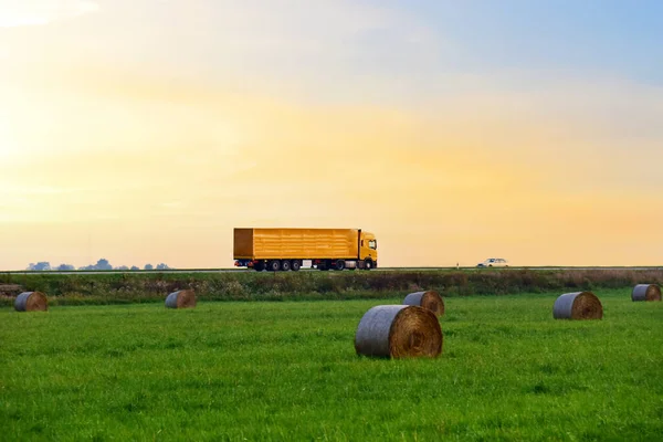 View of a field with hay in rolls against the background of trucks with ...