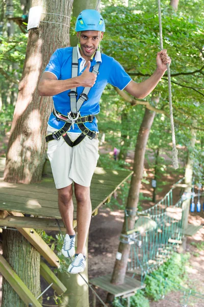 Man showing thumbs up in high rope course - Stock Image - Everypixel