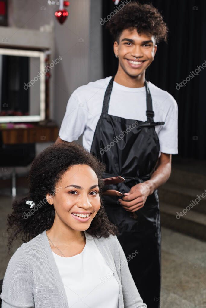 Cliente afroamericano positivo mirando la cámara cerca de estilista con ...