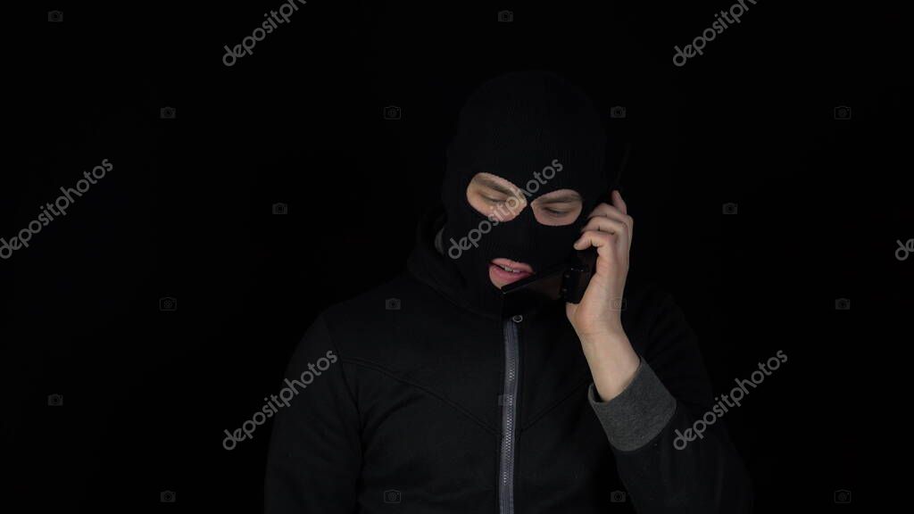 Un hombre con una máscara de pasamontañas está hablando por teléfono ...