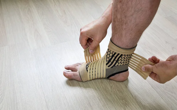 Human hands fix an elastic bandage sock to protect the ankle of the leg ...
