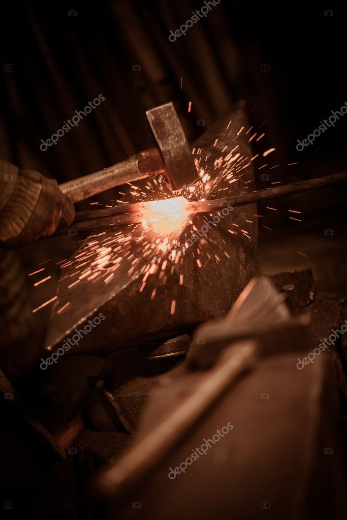 Blacksmith shaping a hot piece of iron on an anvil with a hammer ...
