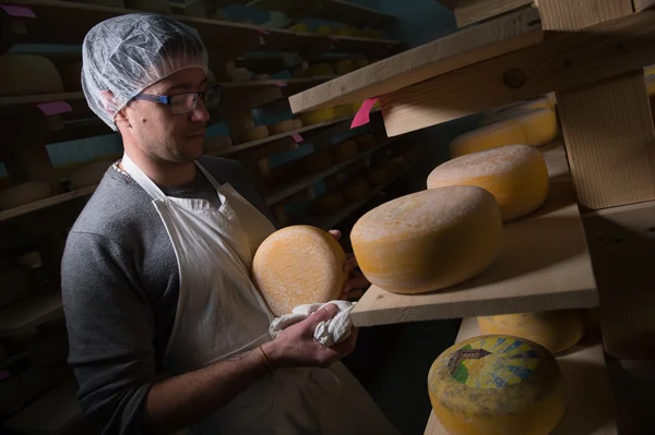 Cheese maker cleaning cheeses in his workshop - Stock Image - Everypixel