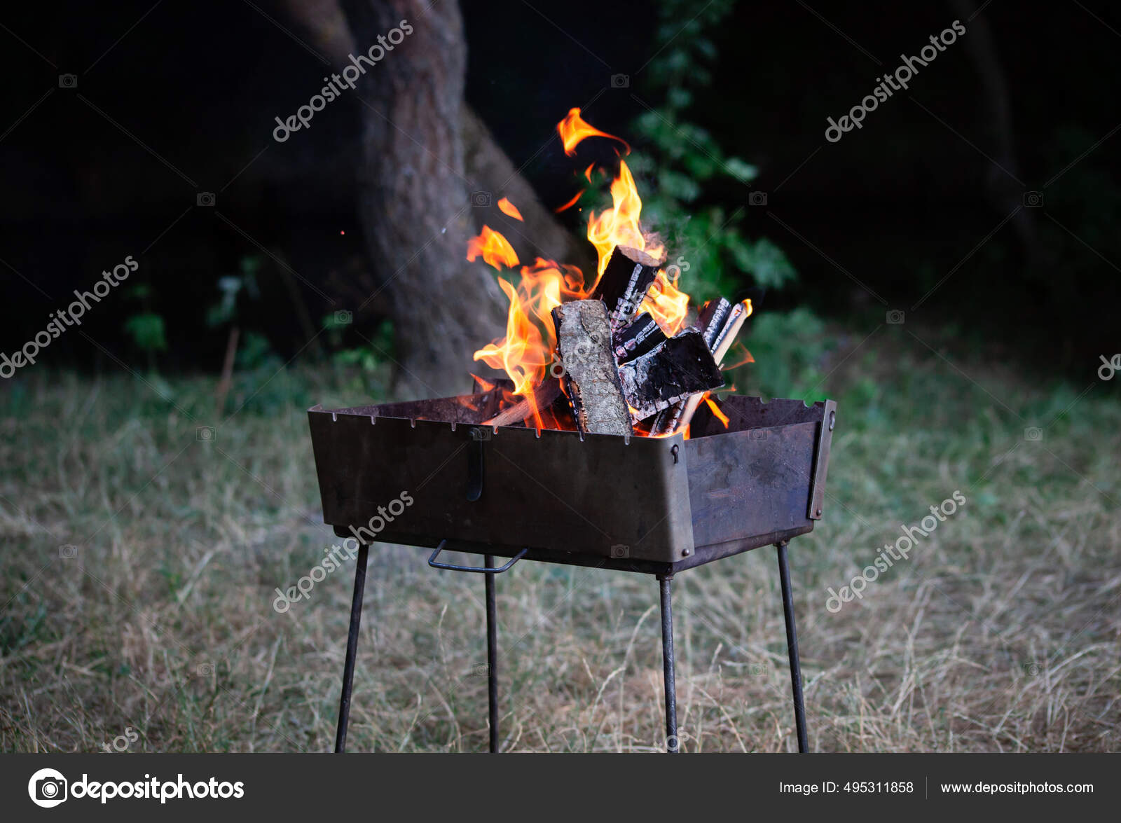 A small folding portable brazier filled with burning wood. Cooking on ...