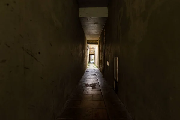 A dark, spooky corridor leading to a lit area with no people. Taken ...