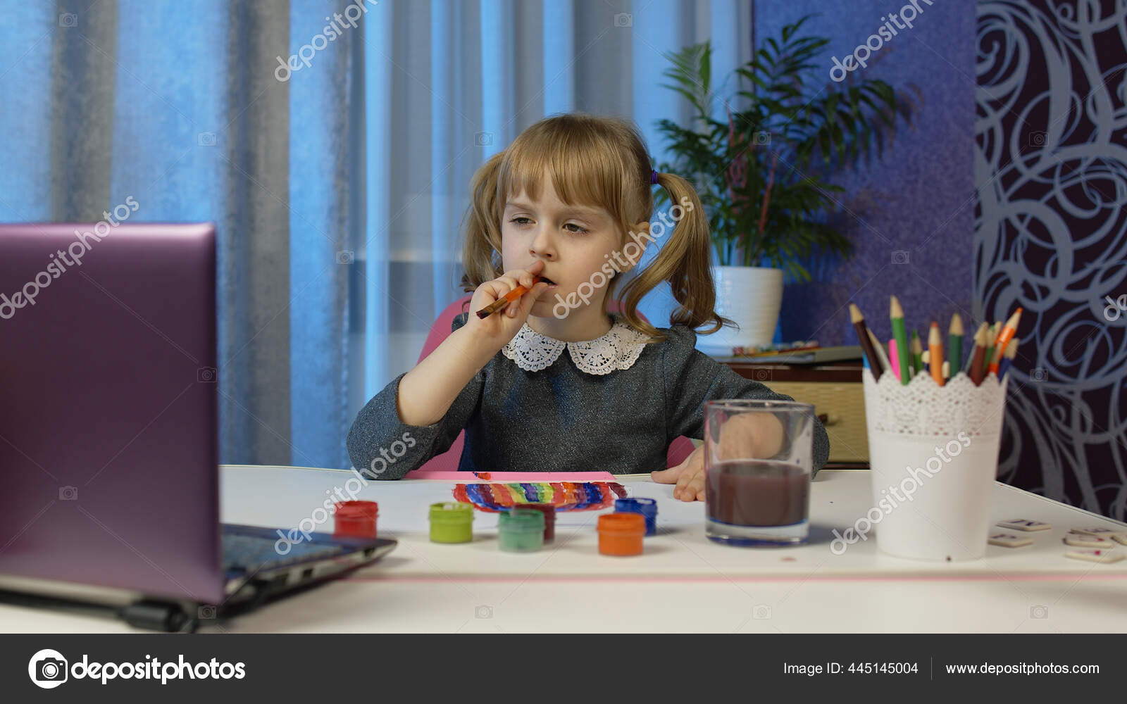 Girl enthusiastically drawing with brushes and paints, using laptop at ...