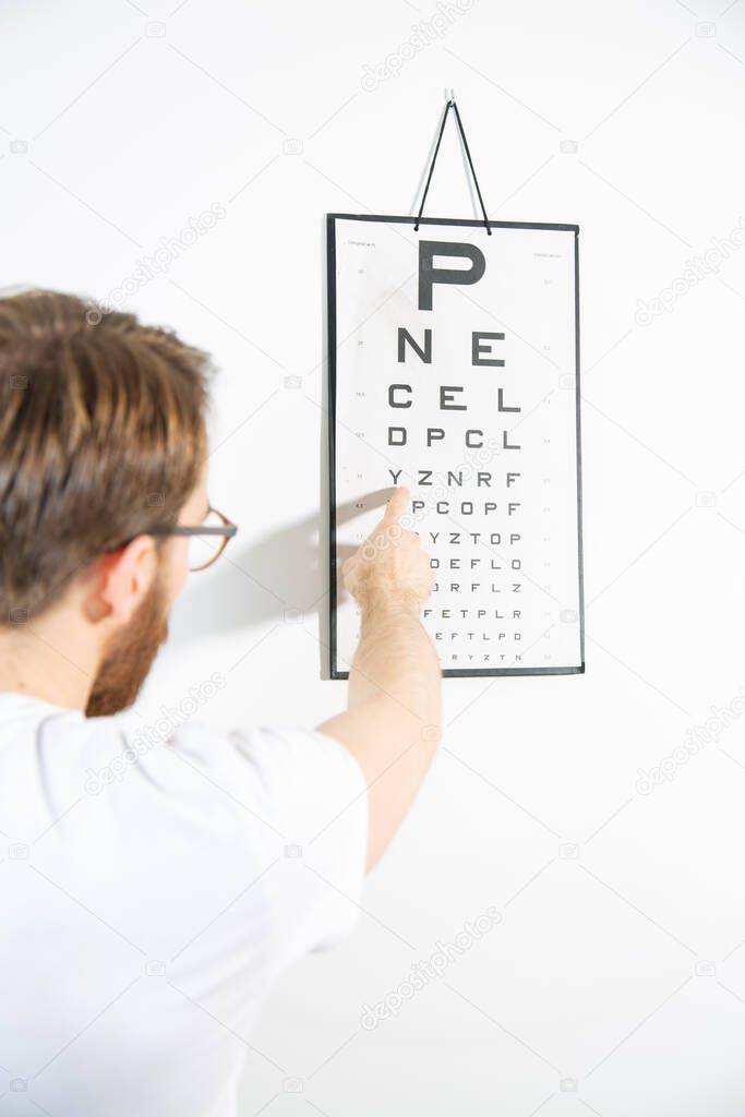 Man reading an eye test chart on a white wall. An ophthalmologist, an ...