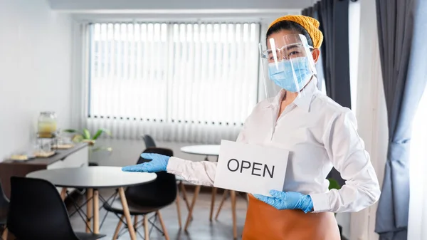 Happy waitress with protective face mask holding open sign for the ...