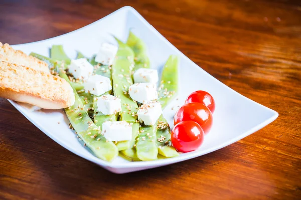 A plate of string beans with feta cheese and sesame seeds, decor ...