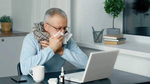 A sick elderly person sits at a laptop and suffers from the flu and a ...