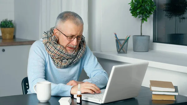 A sick elderly person sits at a laptop and suffers from the flu and a ...