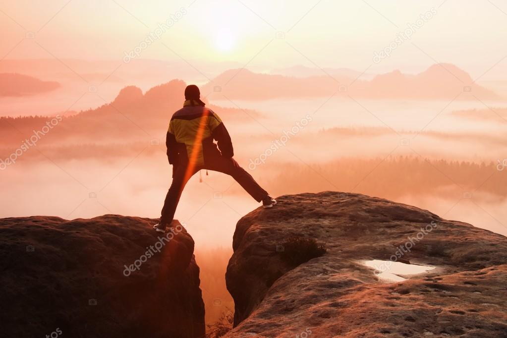 Hiker in black is jumping between the rocky peaks. Wonderful daybreak ...