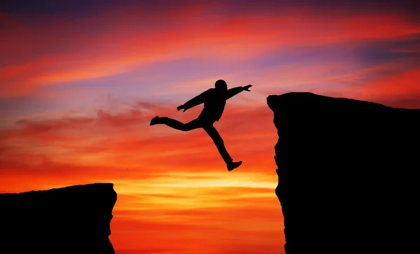 Man jumping across the gap from one rock to cling to the other. Stock ...