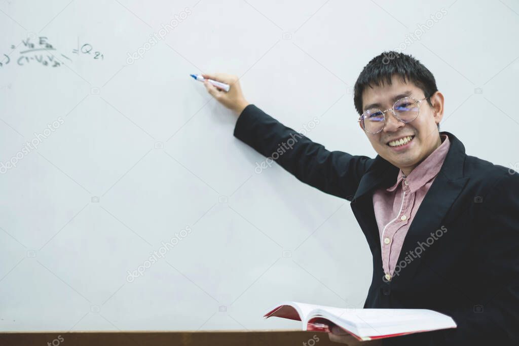 Un profesor asiático en un aula cerca de la pizarra blanca está escribiendo y enseñando una ...