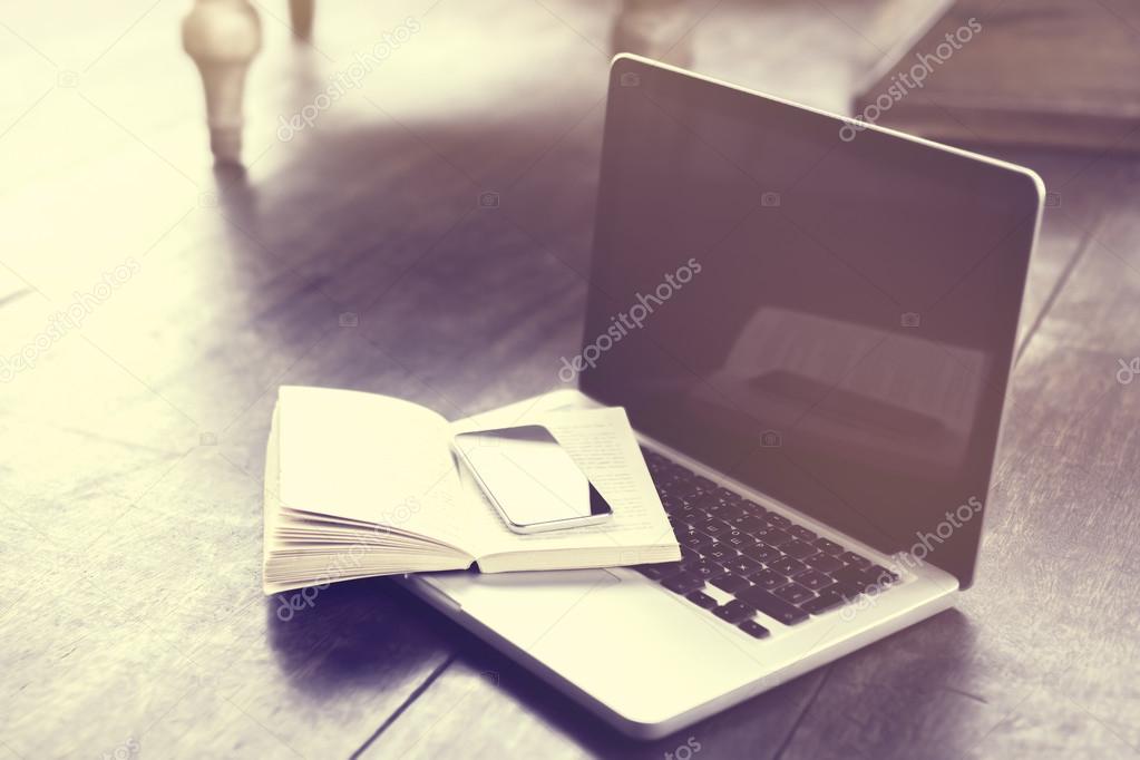 Smartphone on open book and laptop on a floor, vintage photo eff ...