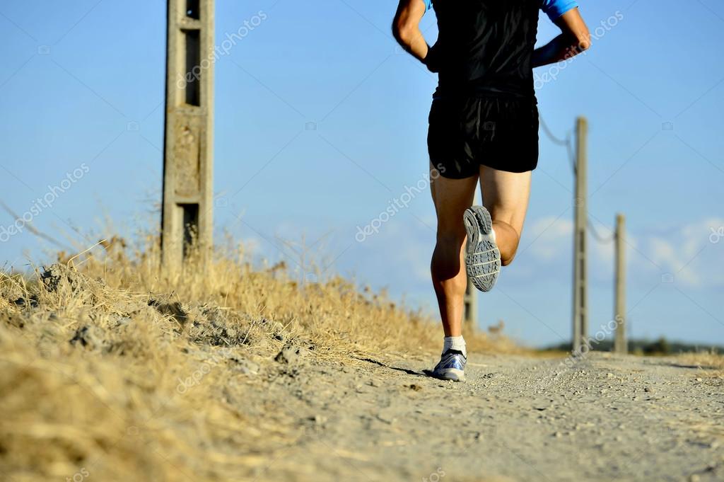 Back view of young sport man legs and feet running on countryside track ...