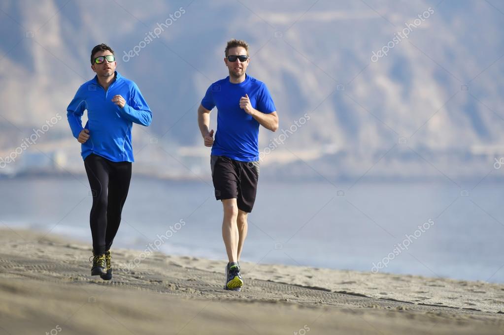 Two men friends running together on beach sand with beautiful coast ...