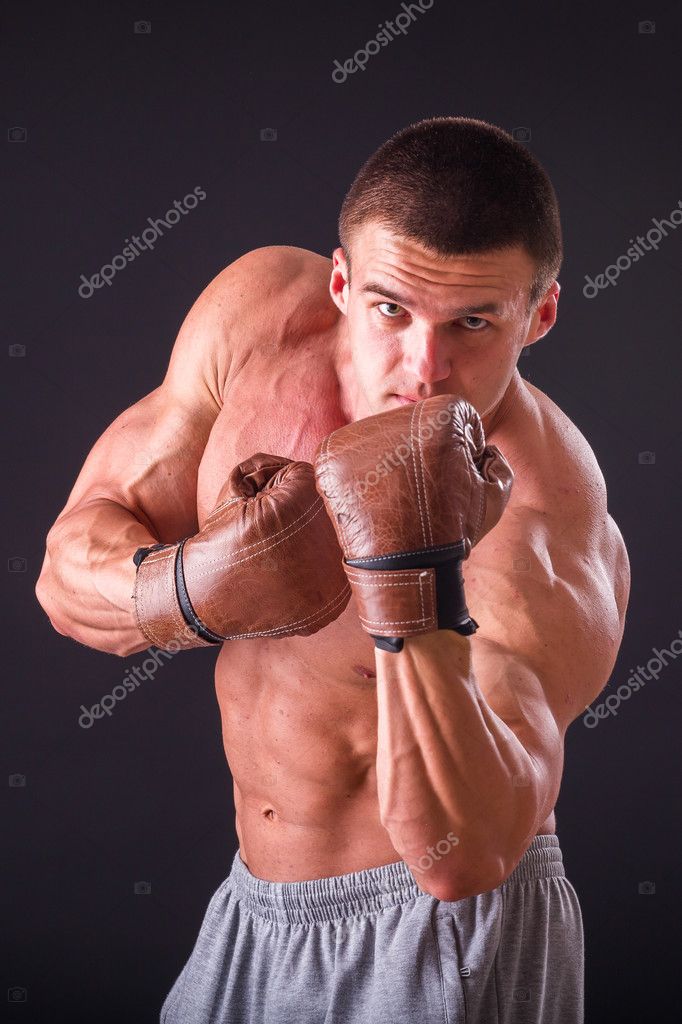 Muscular man in boxing gloves on a dark background. Professional boxer ...
