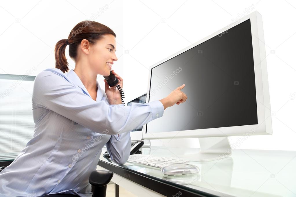 Woman at office desk talking on phone pointing the monitor — Stock ...