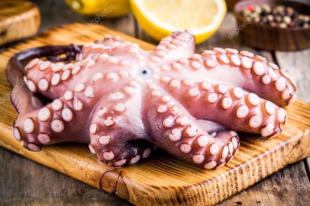 pulpo crudo fresco entero en la tabla de cortar con limón y pimienta 2024