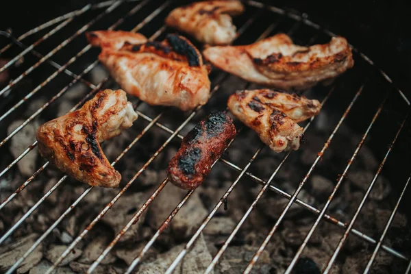 A closeup of beef and chicken wings grilling over a fire pit outdoors ...