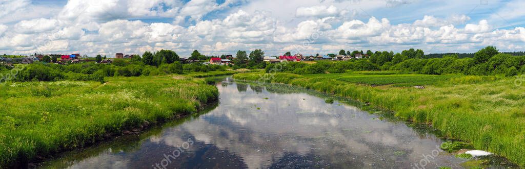 Un río estrecho y tranquilo fluye entre verdes prados. Las nubes se ...