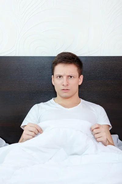 surprised and shocked good looking young man in bed looking down ...