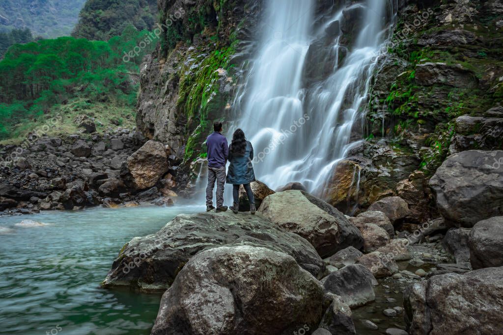 pareja de pie en la roca frente a la cascada corriente de agua blanca ...