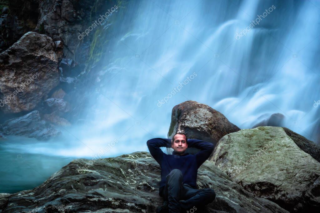 hombre sentado en la roca frente a la cascada corriente de agua blanca ...