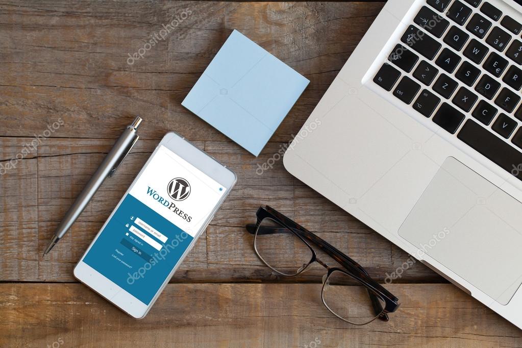 Wordpress app in a mobile phone screen. Top view of wooden desk with ...