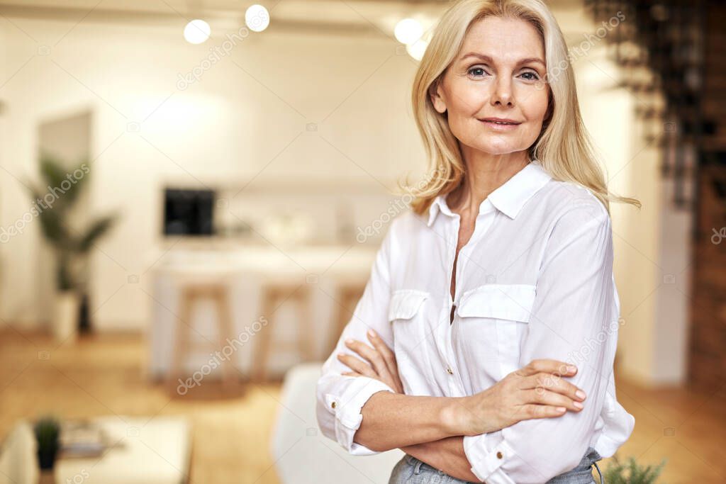 Retrato de una exitosa mujer de negocios rubia madura mirando a la cámara mientras posa, de pie ...