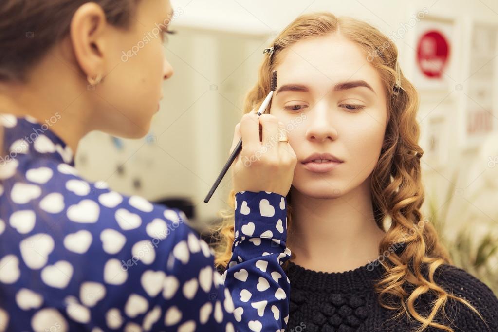 Brunette make up artist woman applying make up for a blonde brid ...