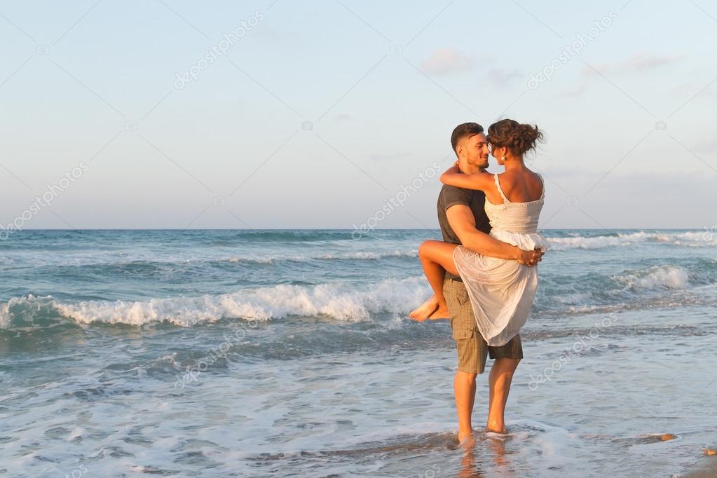 Pareja joven disfruta caminando en una playa nebulosa al atardecer. 2024