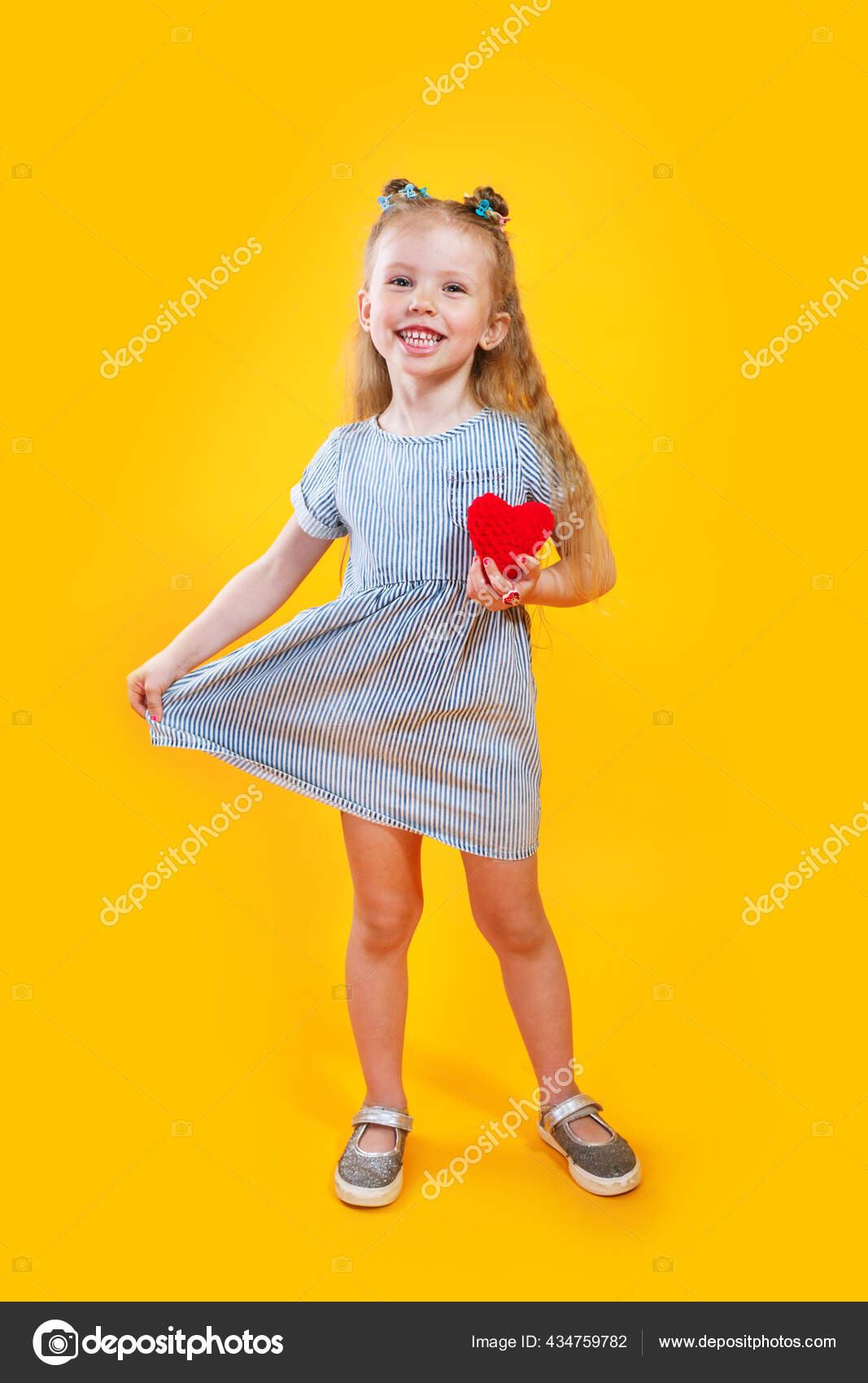 Adorable little model in trendy dress posing with red heart against ...