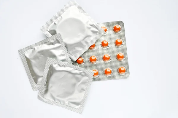 Three condoms and orange birth control pills on wooden table — Stock ...