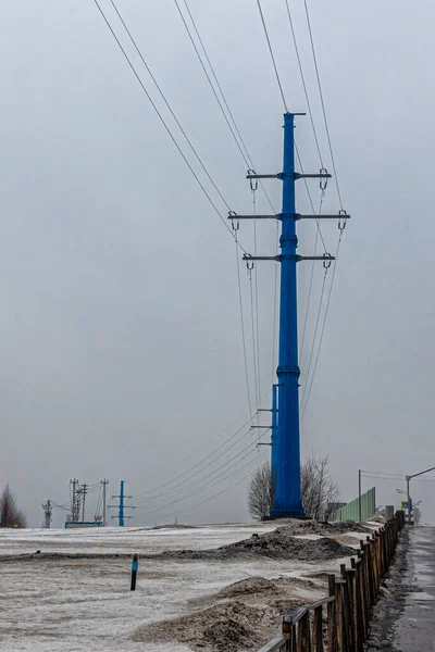 Blue poles of a high-voltage power line in a snow-covered field ...