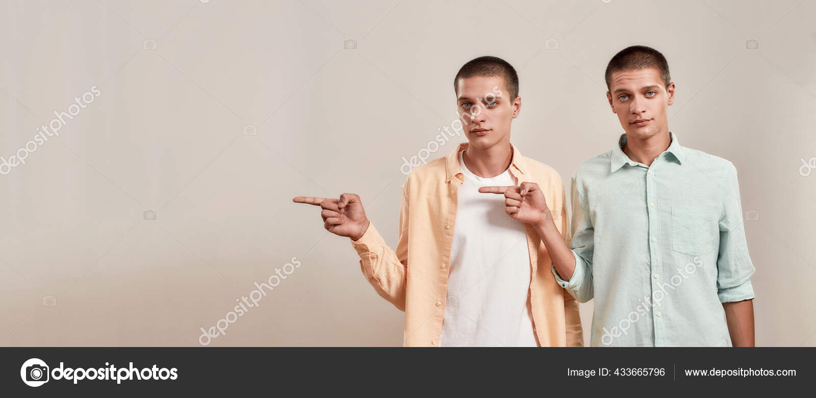 Two young twin brothers in casual wear pointing to the left and looking ...