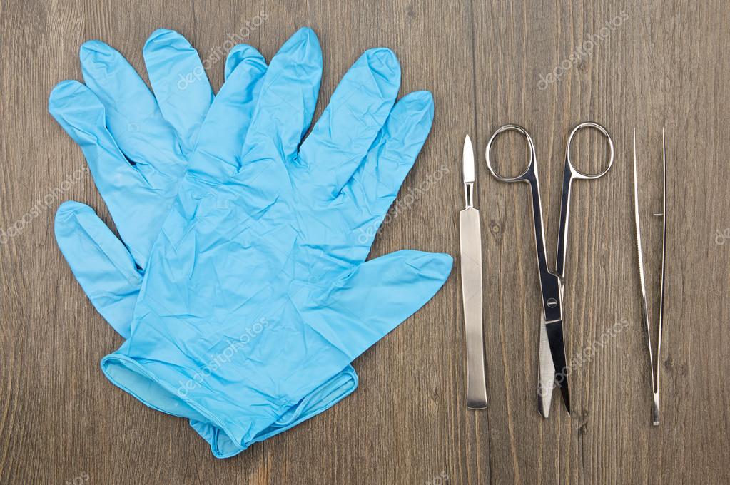 Silver scalpel surgical scissors and forceps beside blue latex glove ...