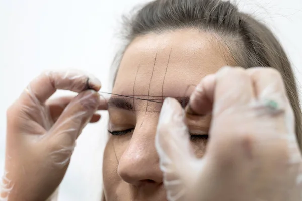 Permanent makeup, eyebrow tattoo. The master draws lines with a thread ...