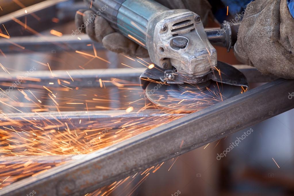 Factory worker using electric grinder machine cutting metal. Sparkles ...