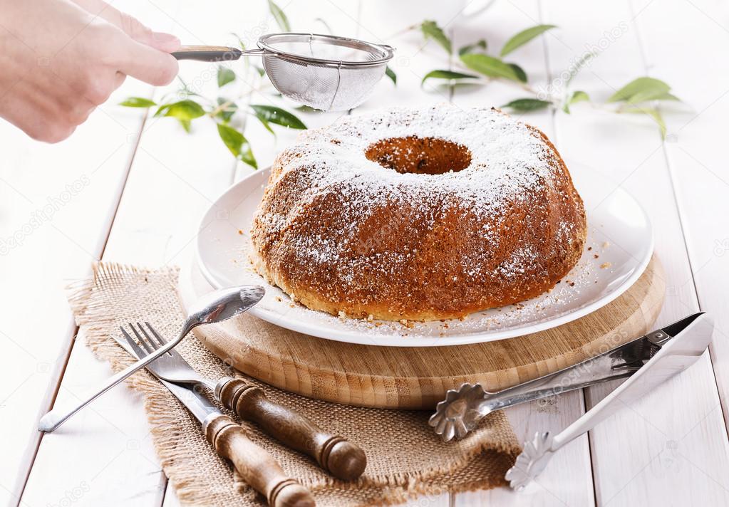 Baker hand dusting Bundt Cake with icing sugar Stock Photo by ©Yulia ...