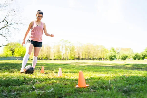 Portrait of young female soccer player running around cones while ...