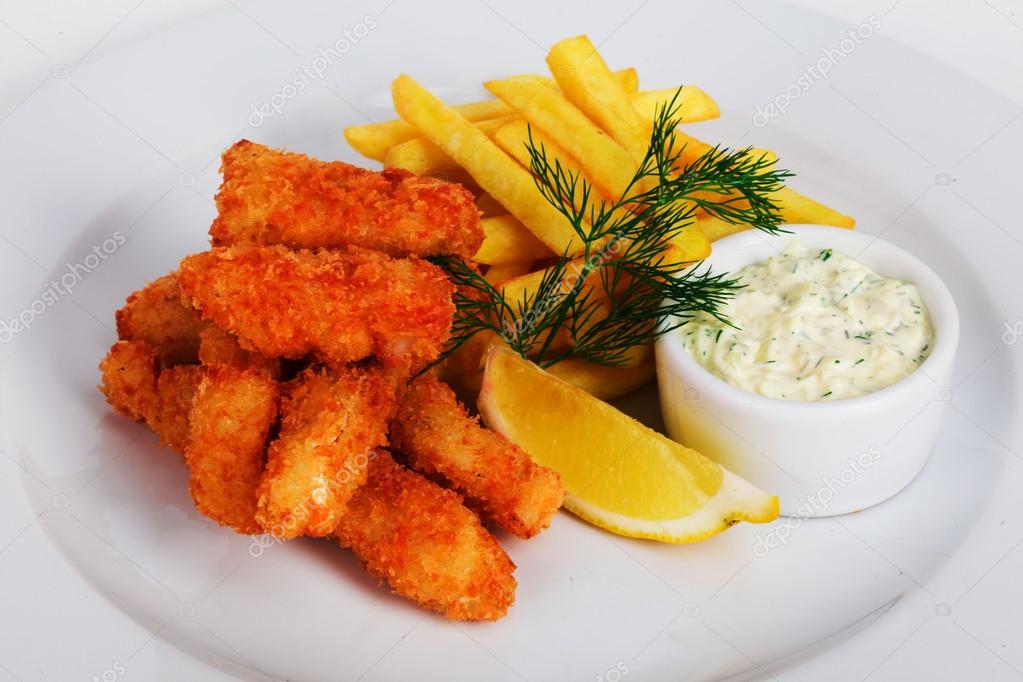 Breaded fish sticks with french fries, lemon, dill and sauce on a plate ...