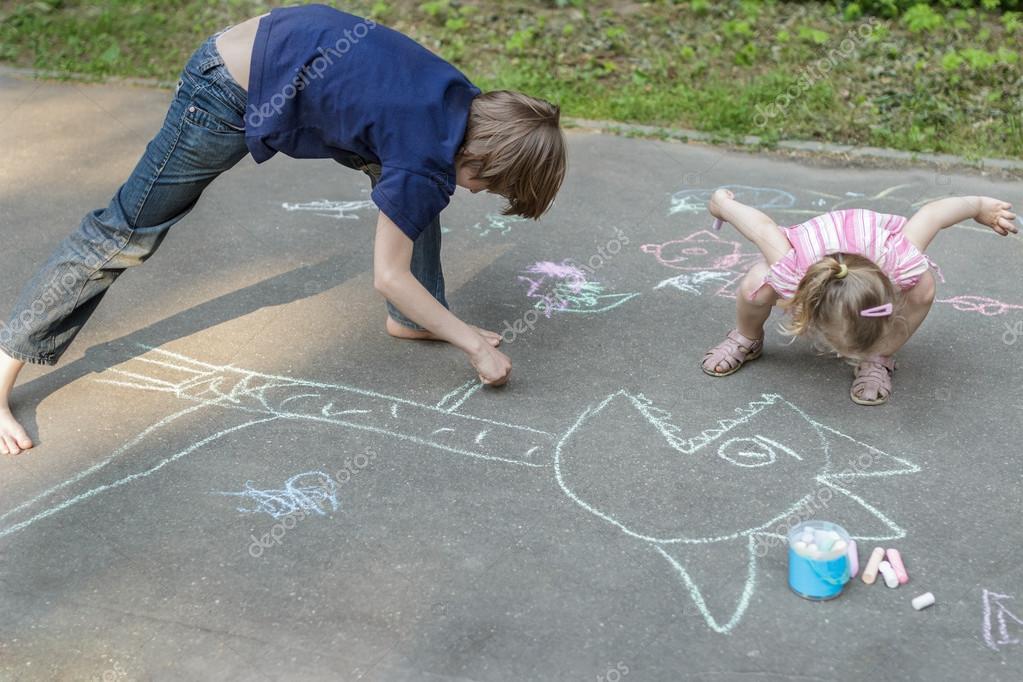 Sibling children playing during sidewalk chalking on asphalt surface ...