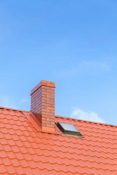 Faded red metal roof tile, rain gutter and chimney against blue sky ...