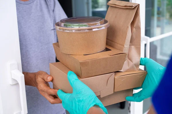 A gloved employee is sending food boxes to customers on the doorstep ...
