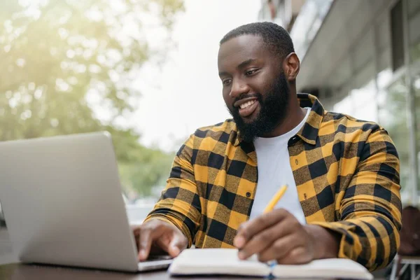 Young handsome African American man using laptop computer, taking notes ...